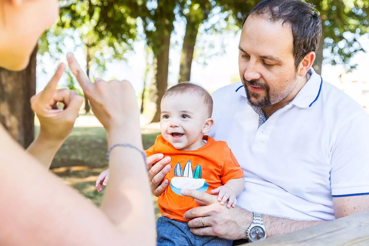 Père tenant bébé, à l'extérieur, mère communiquant avec bébé à l'aide des mains