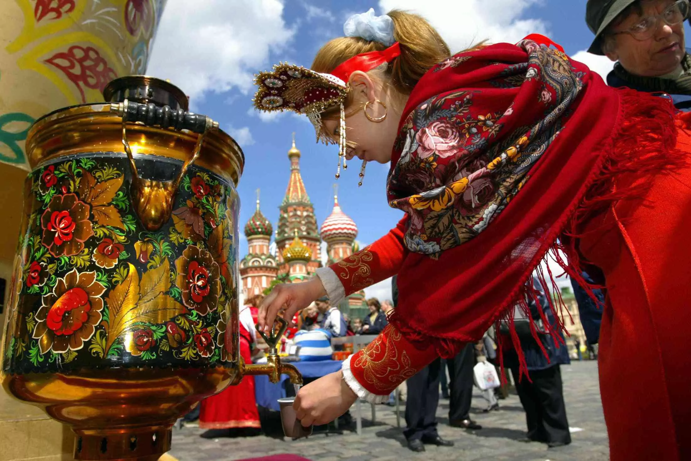 Russisch meisje dat traditionele kleding draagt, giet water uit samovar