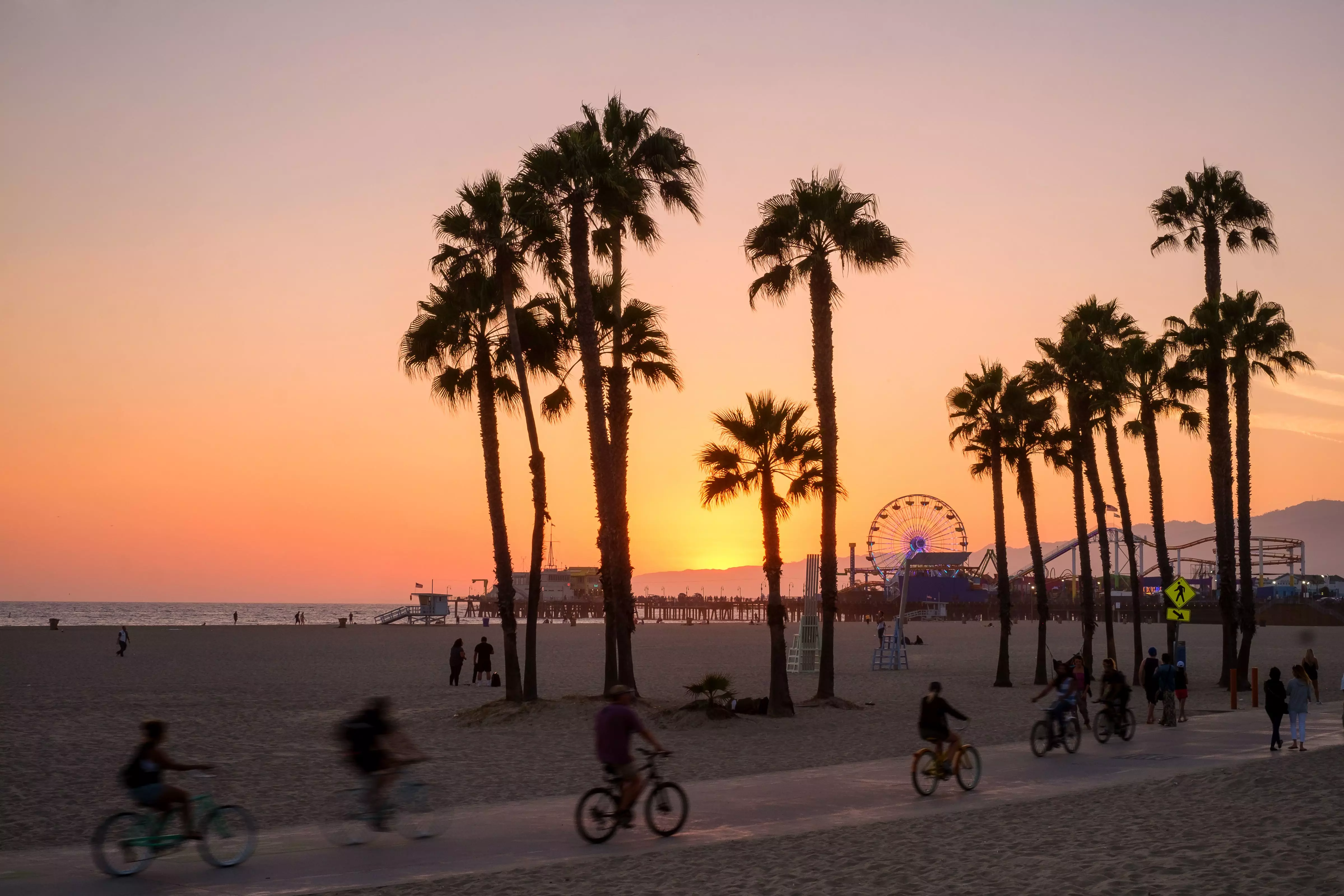 Orang-orang mengendarai sepeda dan berjalan di sepanjang pantai saat matahari terbenam di Santa Monica, California.