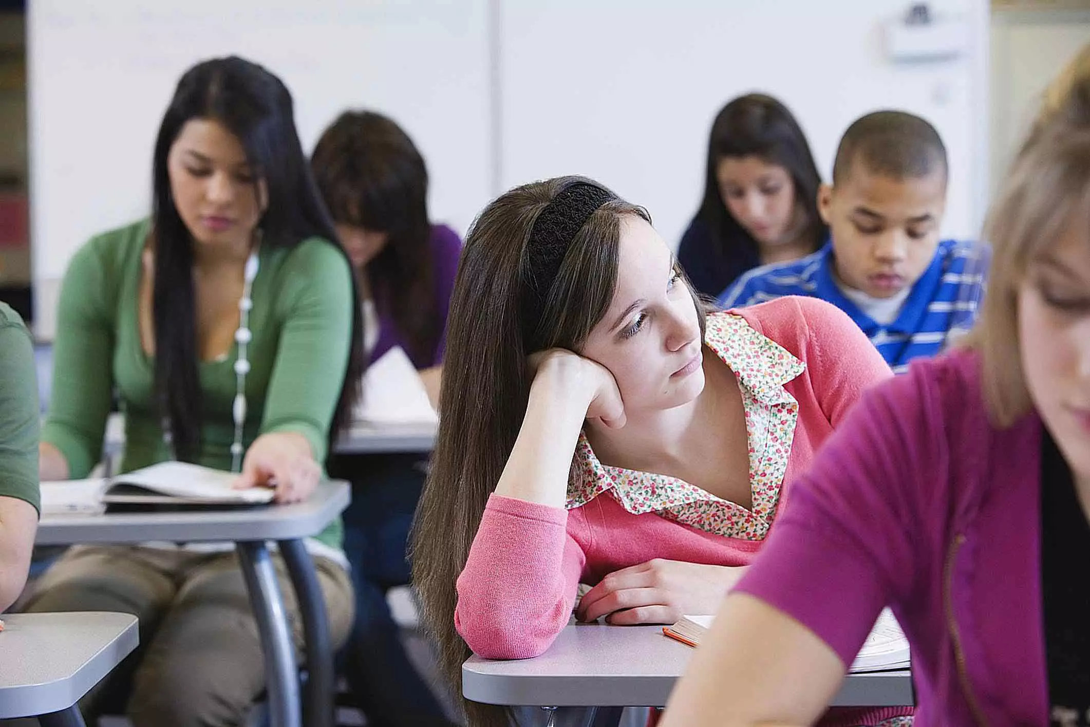 Gadis remaja (16-17) duduk di kelas, memalingkan muka