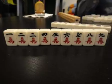 Bir masanın üzerinde duran Mahjong çinilerinden oluşan karakter takımı.