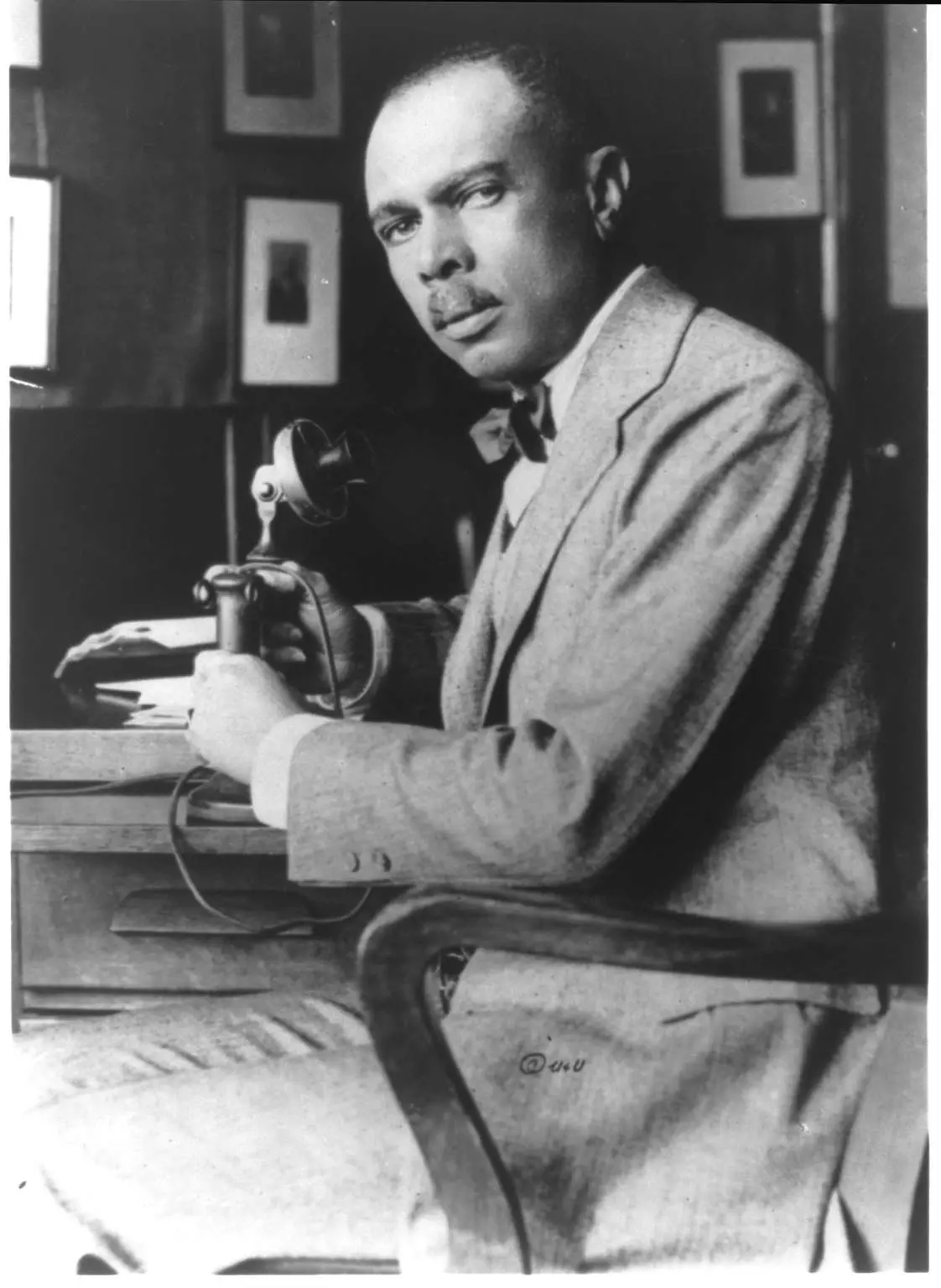 James Weldon Johnson អង្គុយនៅតុរបស់គាត់ រូបថតសខ្មៅ។