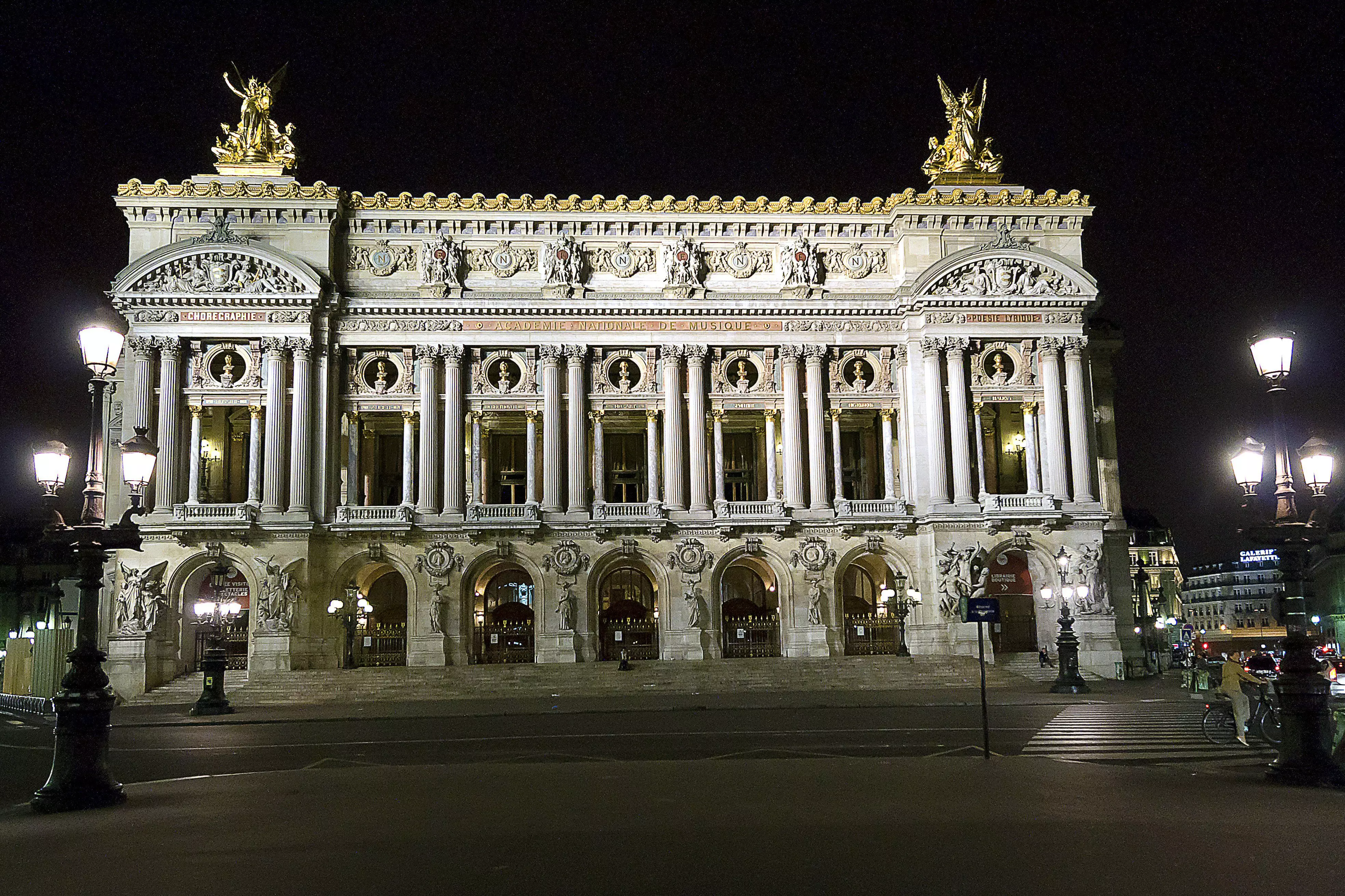 esterno altamente decorato di un edificio rettangolare a forma di scatola con archi e colonne e sculture illuminate di notte