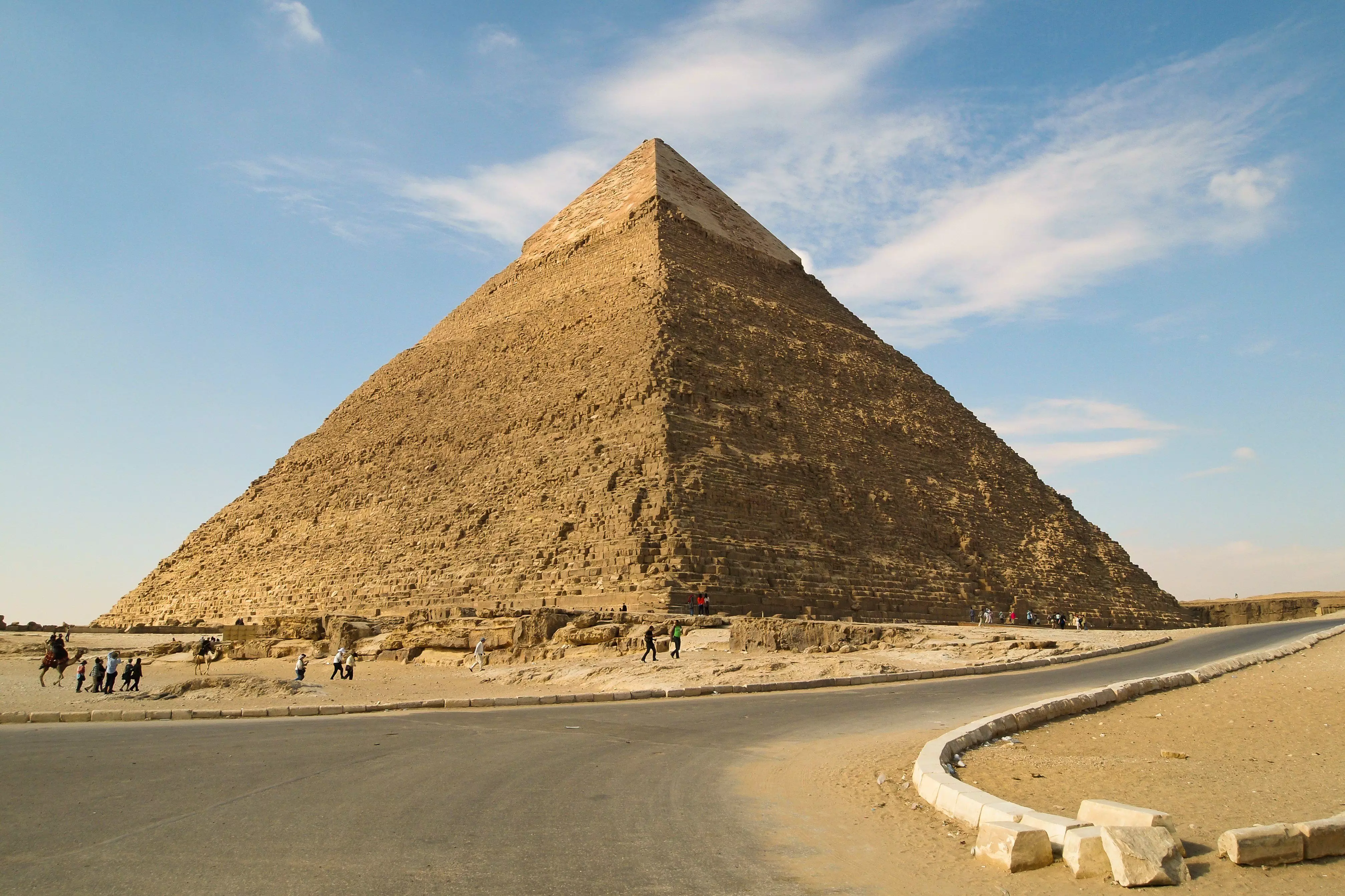 cielo blu, grande piramide marrone vicino alla strada e piccole persone e figure di cammelli