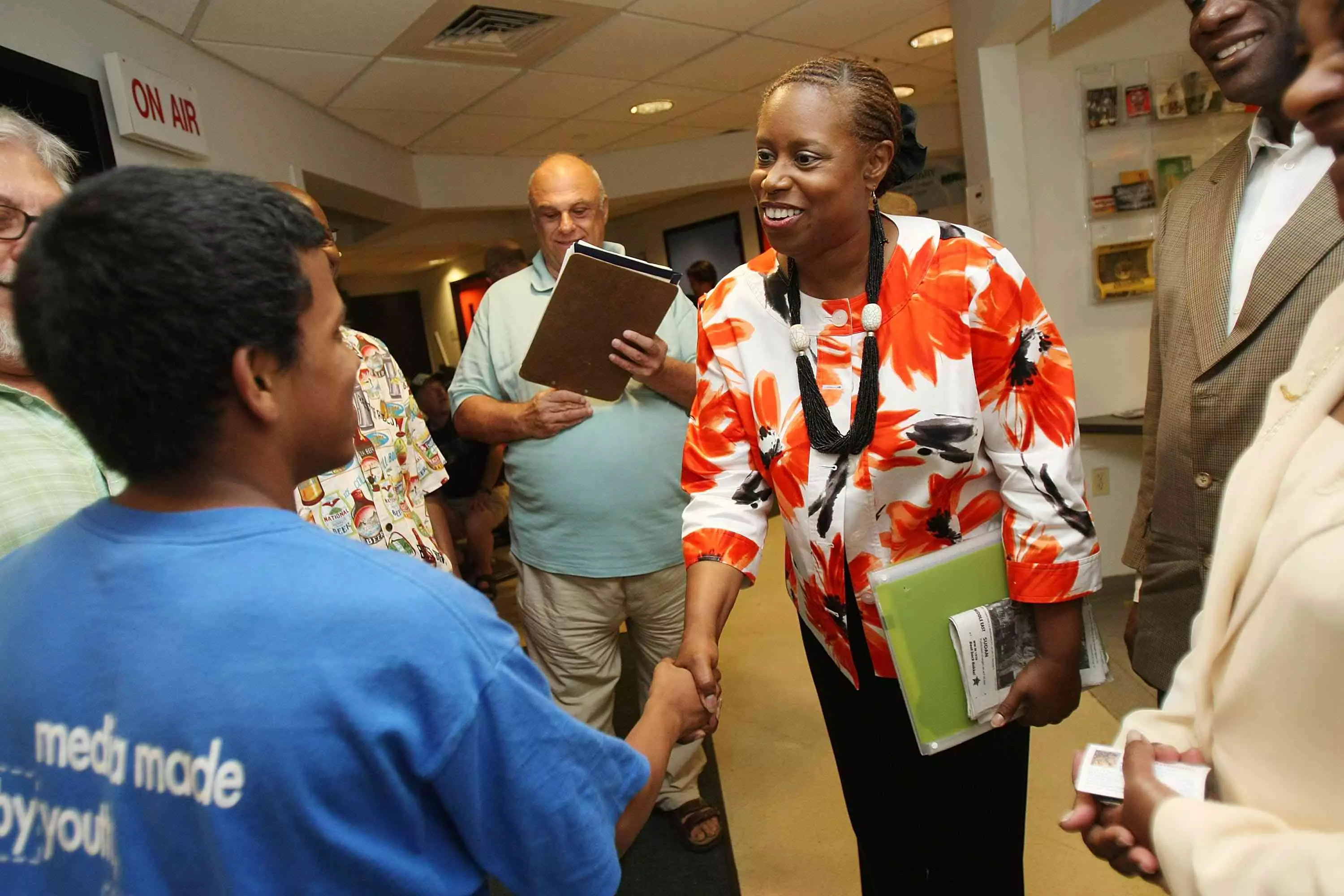 Cynthia McKinney portant un chemisier orange et blanc serrant la main d'un homme et souriant dans un cercle de personnes