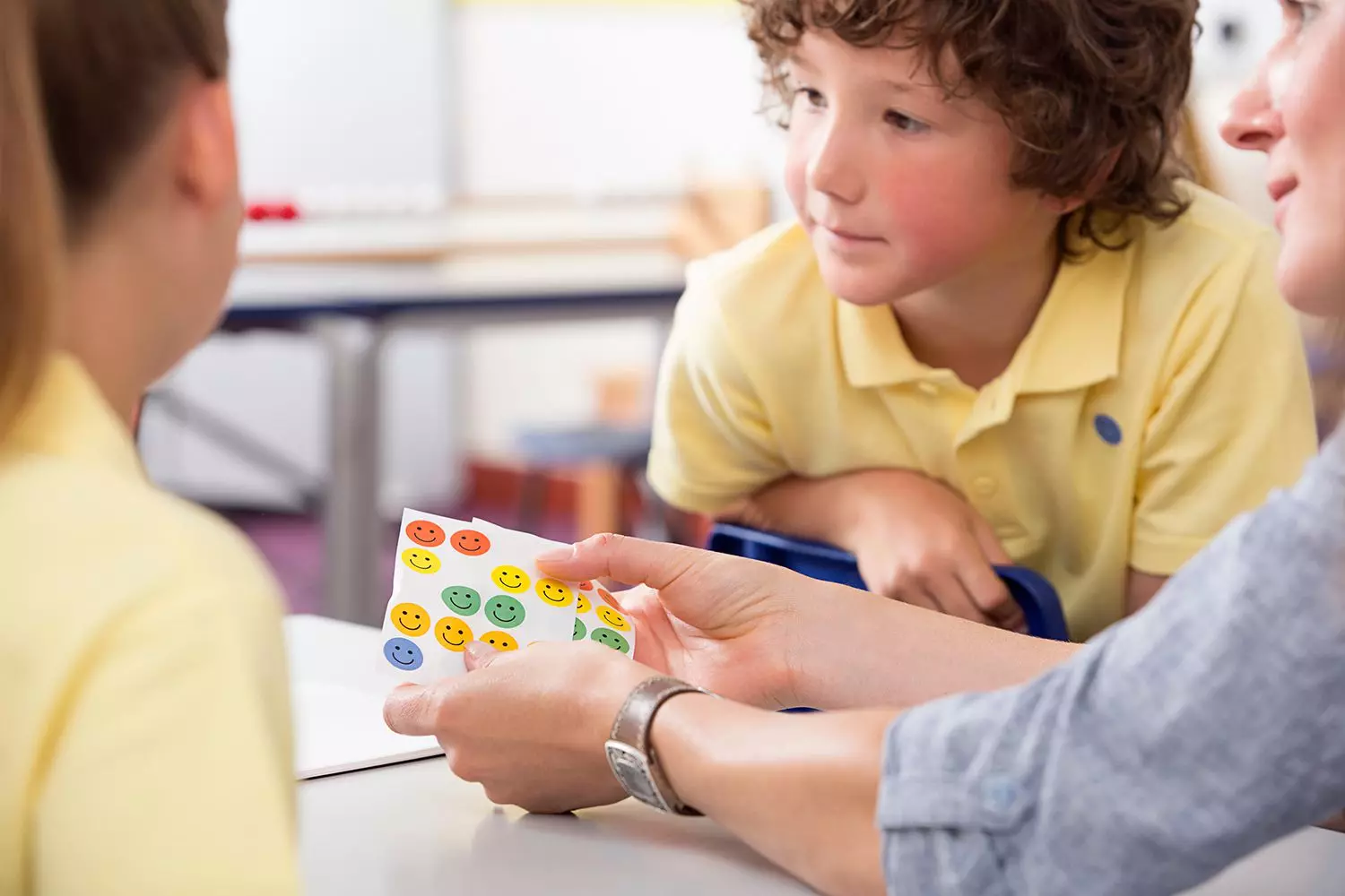 Onderwyser gee glimlaggesig-plakkers aan laerskoolleerlinge