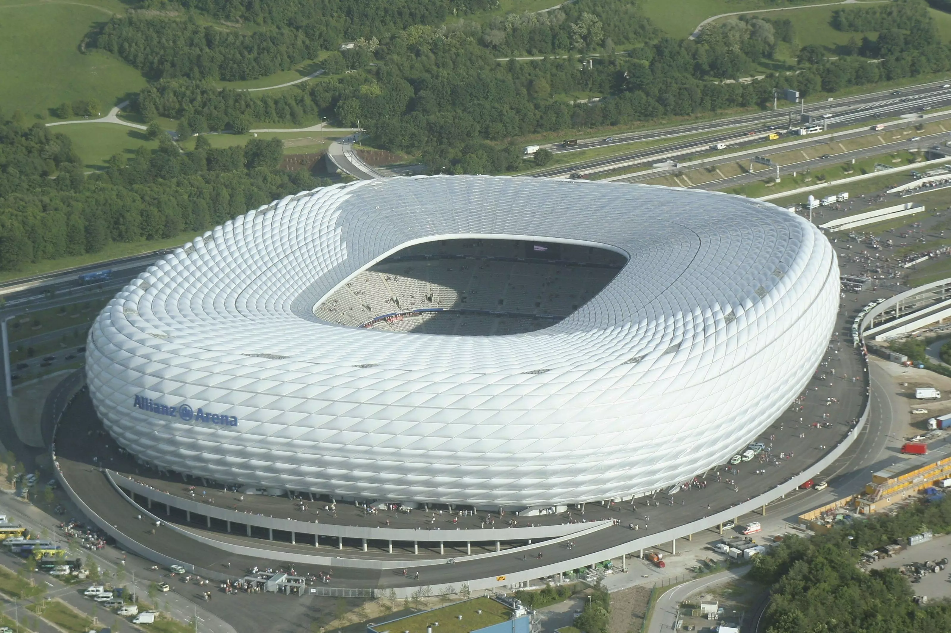 大きな丸みを帯びた正方形のスタジアム、彫刻が施された白、アリアンツアレーナの看板、オープンエアセンターの航空写真