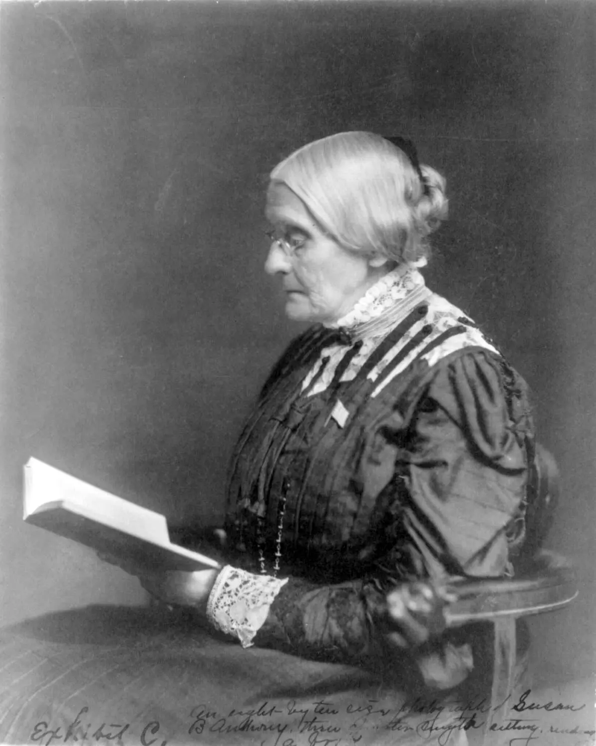 Susan B. Anthony, yn eistedd, yn wynebu'r chwith, yn darllen.