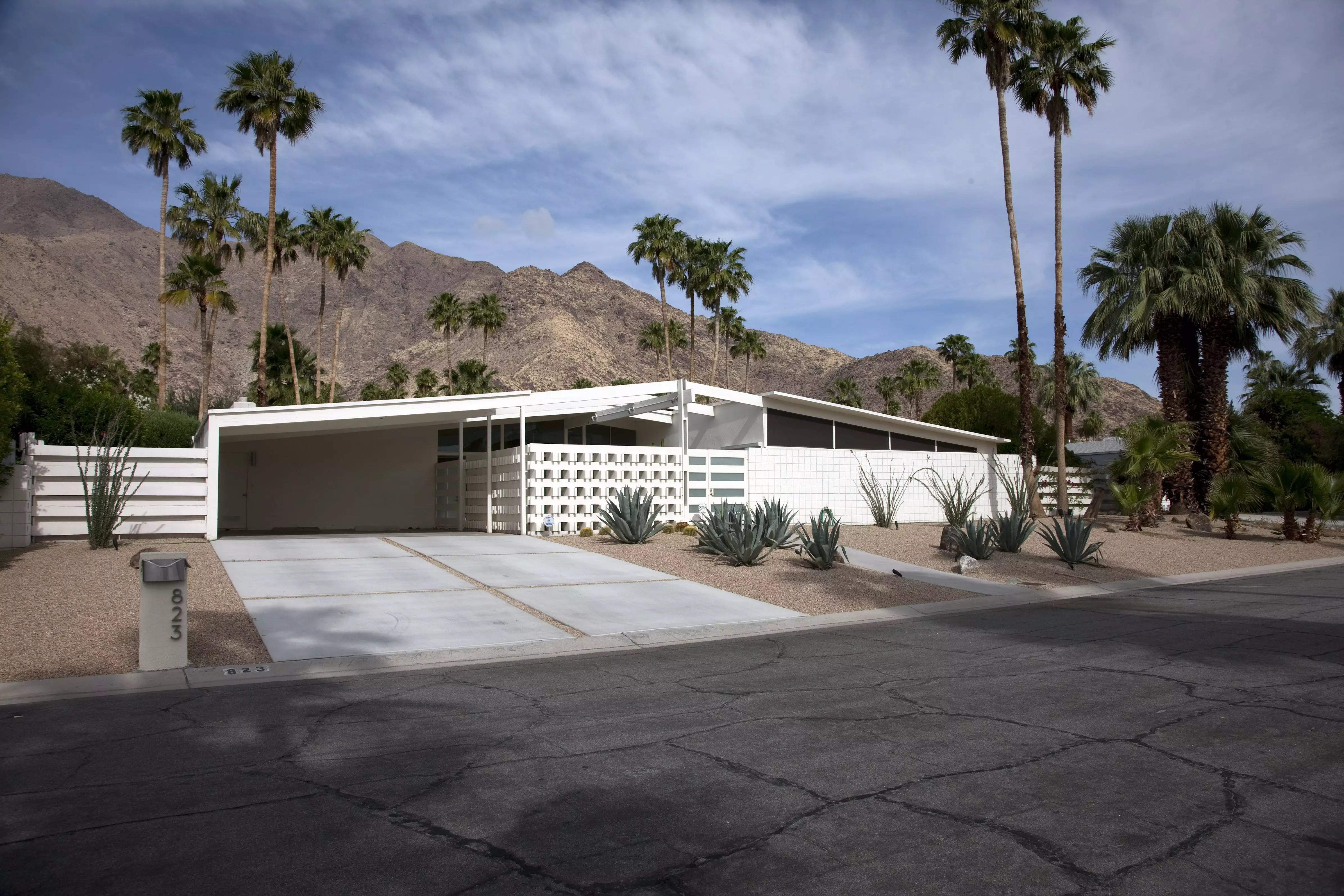 Modernes, horizontal orientiertes weißes Haus mit offenem Carport, Schrägdach und unter felsigen Hügeln gelegen