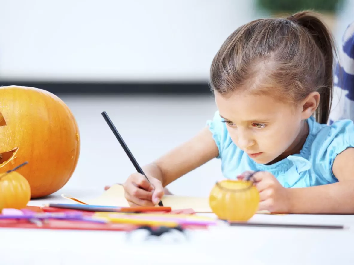 Ib tug hluas nkauj sau rau ntawm lub rooj nrog lub jack o' lantern ntawm nws..