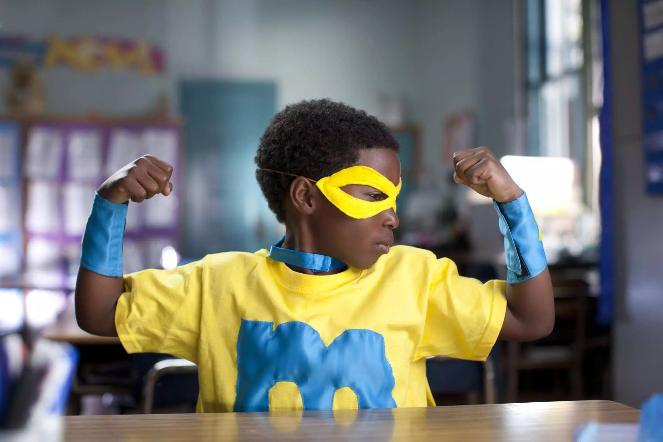 Un garçon en costume de super-héros assis à son bureau d'école.