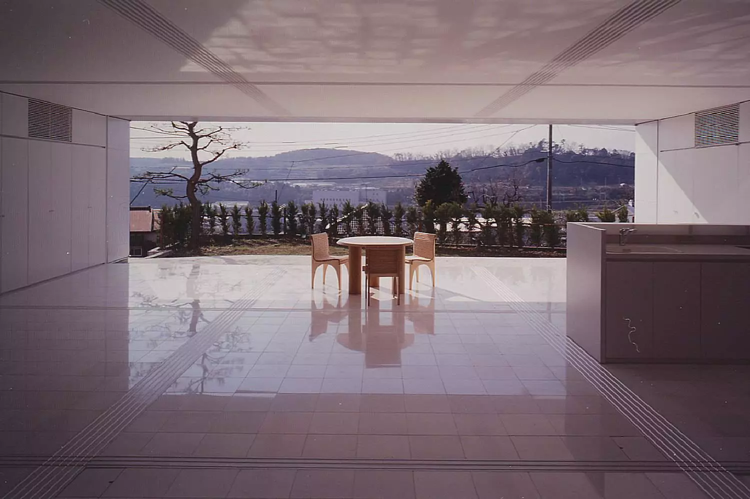 kahles Zimmer mit Tisch und Stühlen, glänzende Oberflächen mit Rillen, eine Wand fehlt mit Blick auf die Berge