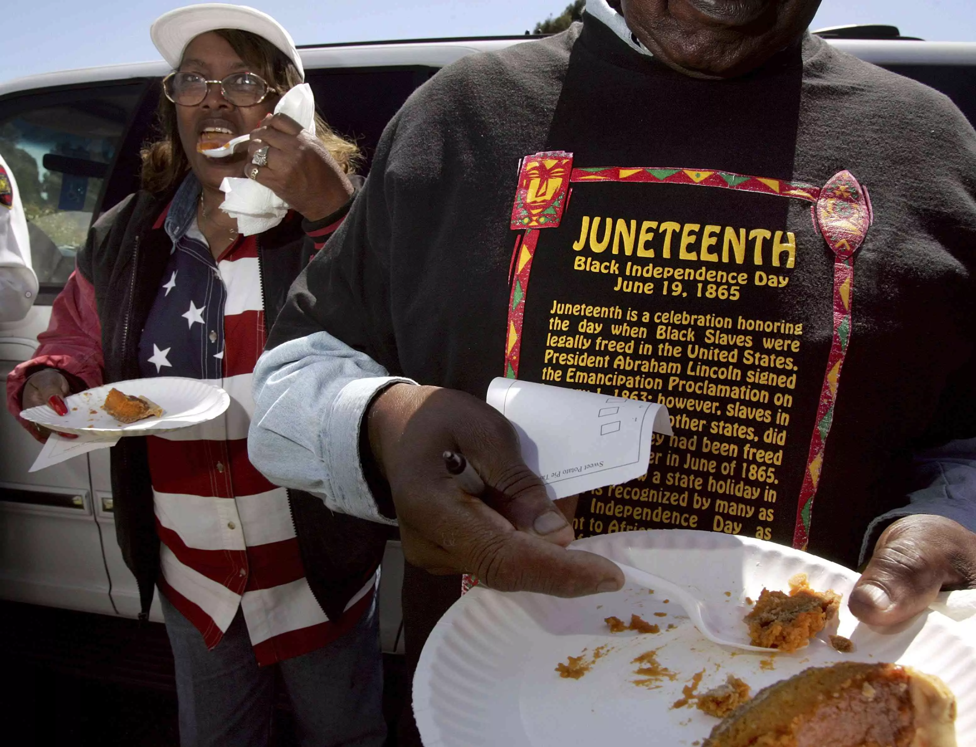 Vrouw draagt shirt met Amerikaanse vlag en eet naast man met shirt over Juneteenth en eet