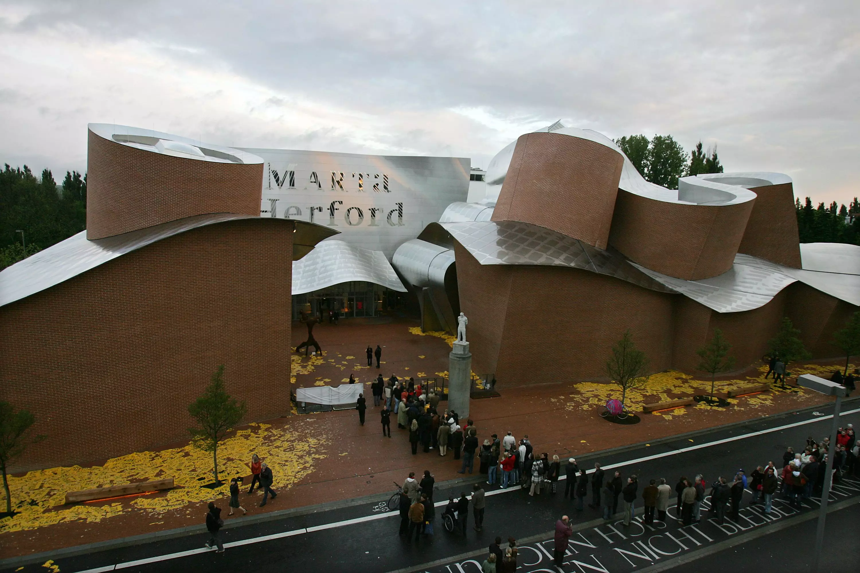 laang Vue vum gewellte Metalldach op roude Mauer Gebai mam Numm MARTa Herford - D'Leit stinn op fir de 'MARTa' Musée de 7. Mee 2005 zu Herford, Däitschland anzeginn. De Musée fir zäitgenëssesch Konscht an Design, entworf vum US-Stärenarchitekt Frank Gehry, bitt en Ausstellungsraum vun 2.500 Quadratmeter a gouf no enger Bauzäit vu véier Joer fäerdeg.