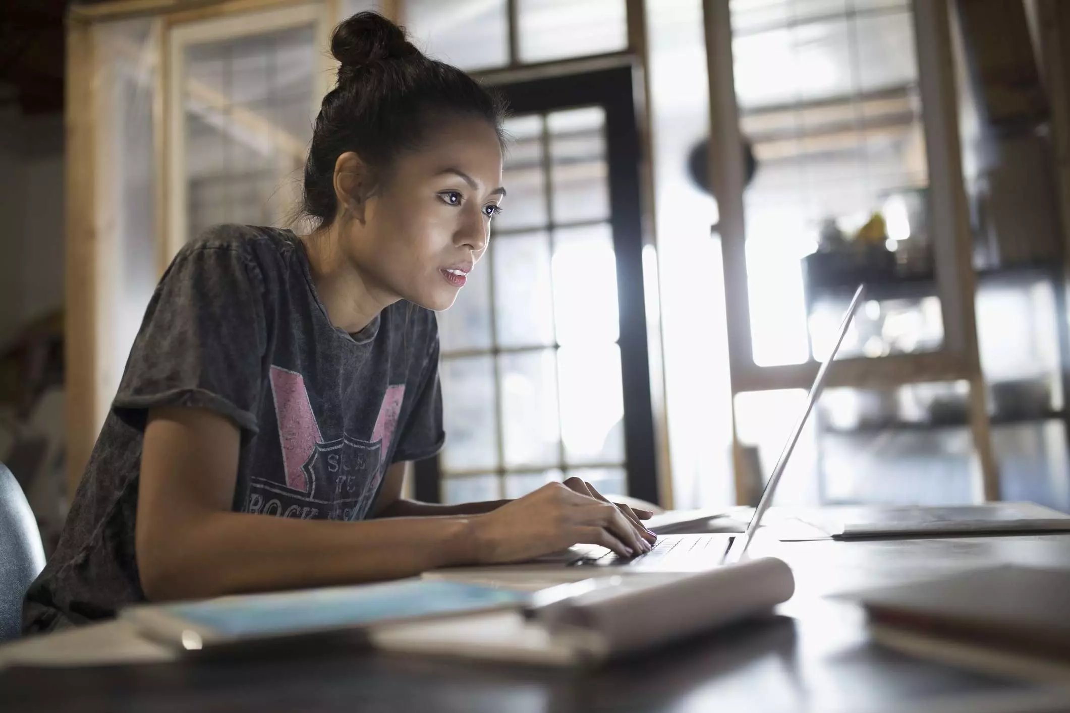 Wanita muda yang fokus bekerja di laptop di kantor