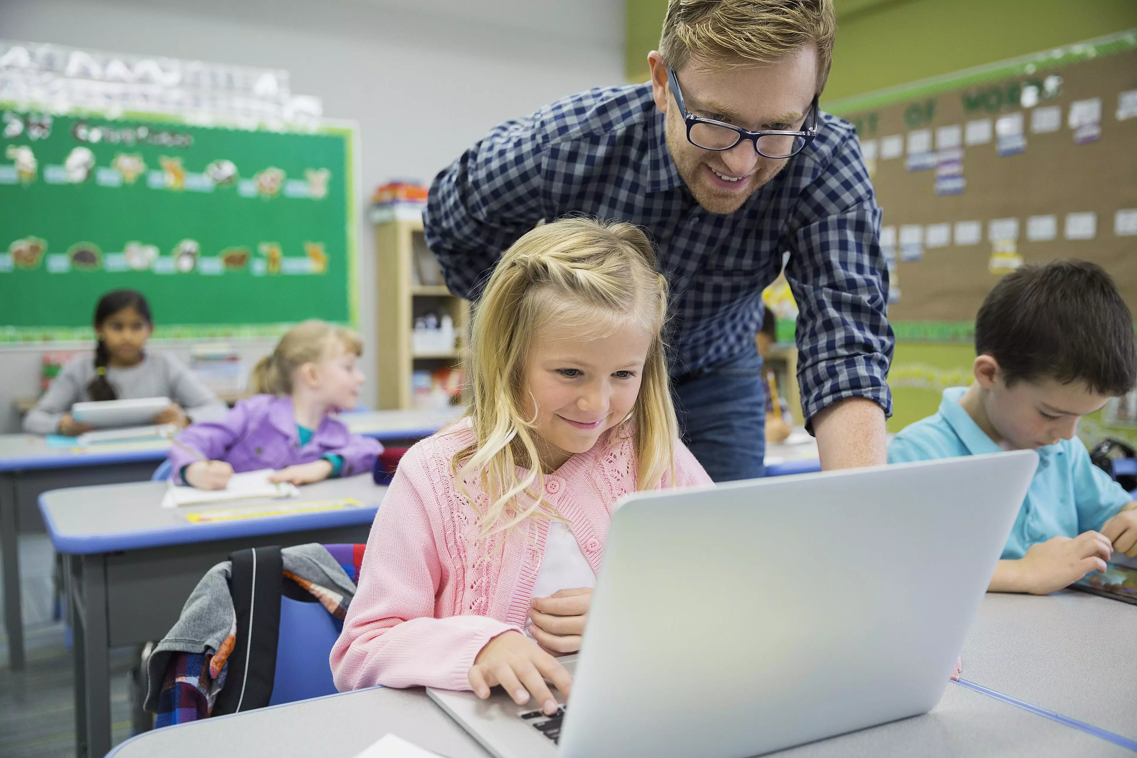 Nauczyciel i uczeń szkoły podstawowej korzystający z laptopa w klasie