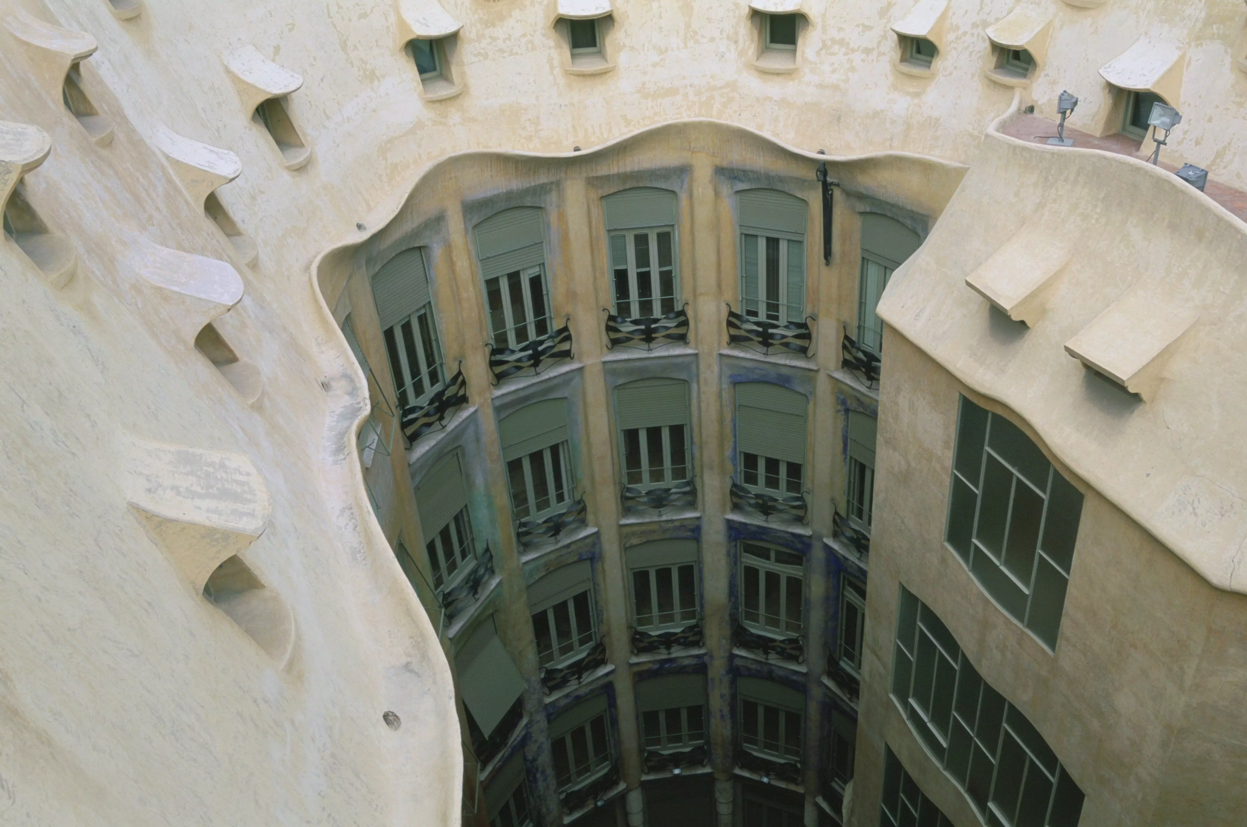 снимка детайл на екстериора на сградата, гледан от извит покрив с капандури, гледащ стена от прозорци в кладенец на стена на сграда