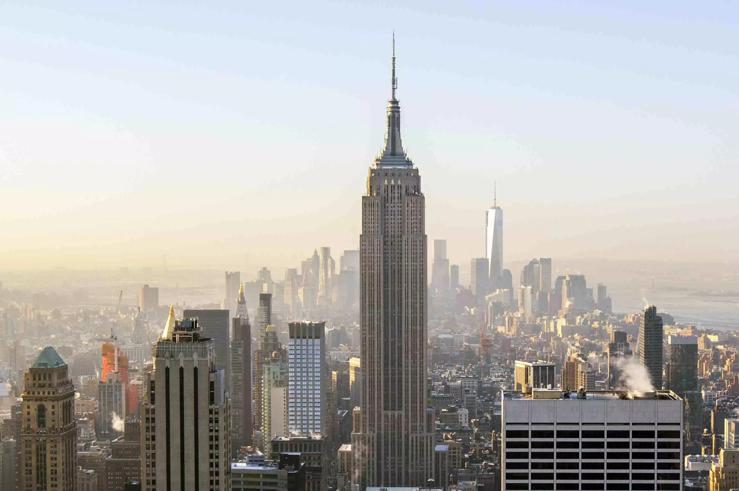 ser en by skyskrabere, stor trappeskyskraber i midten og sølvfarvet skyskraber i baggrunden, ser mod Lower Manhattan