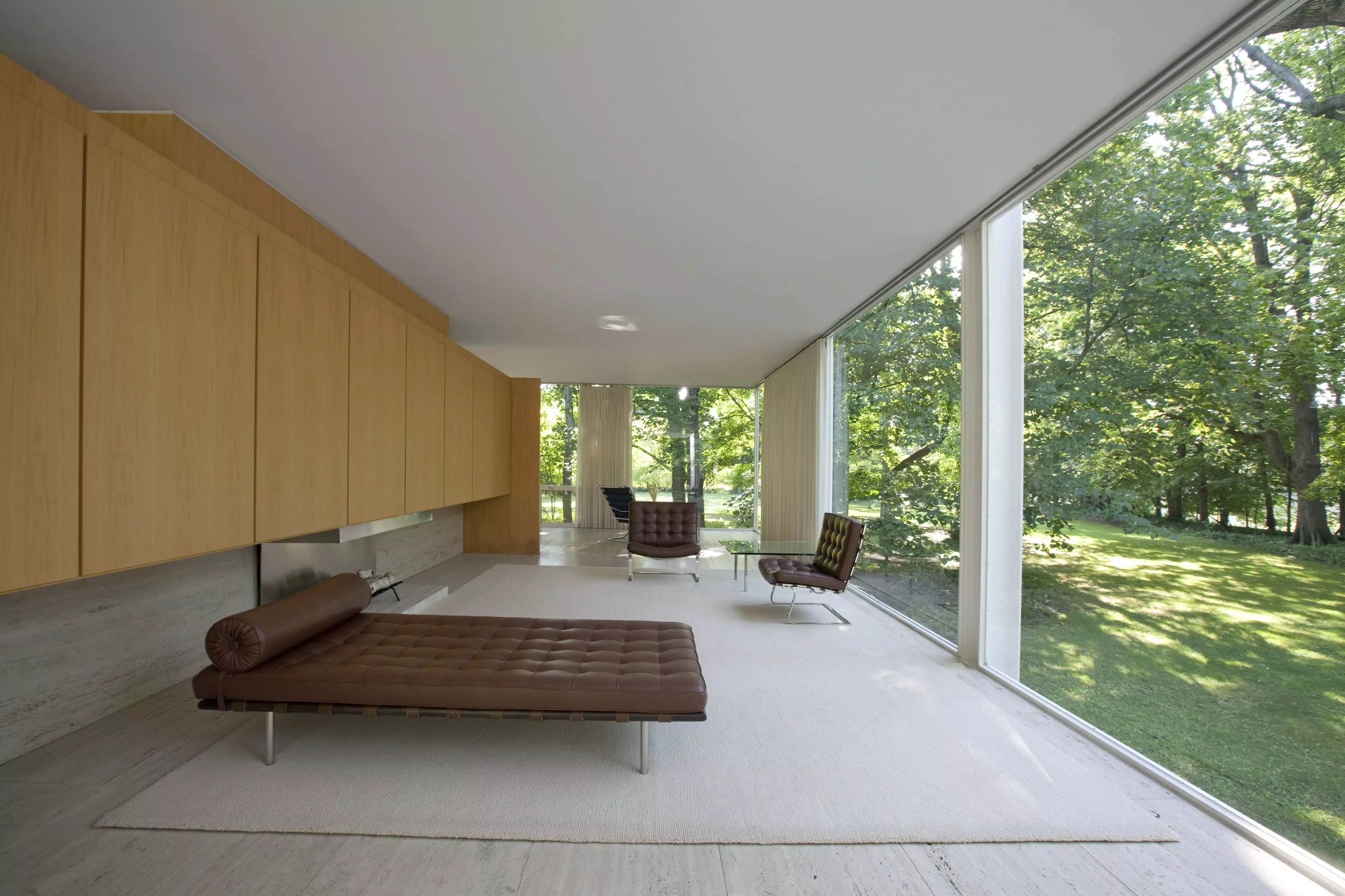 invändig vy av skarpt modernt sovrum med en vägg av fönsterglas genom vilken grönska ses