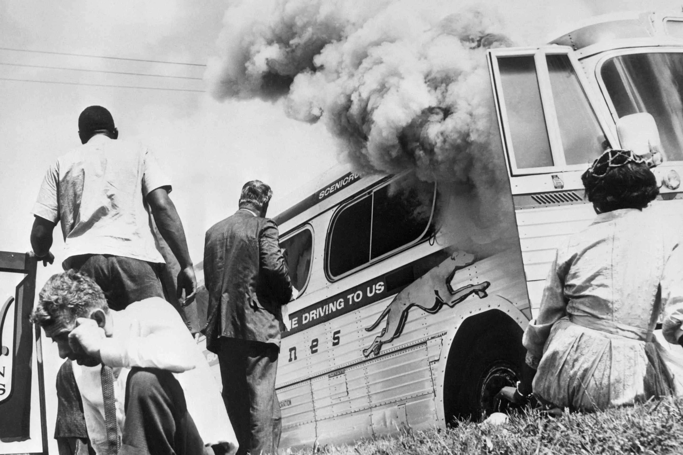 Freedom Riders sitter og står utenfor bussen mens det kommer røyk ut av vinduene