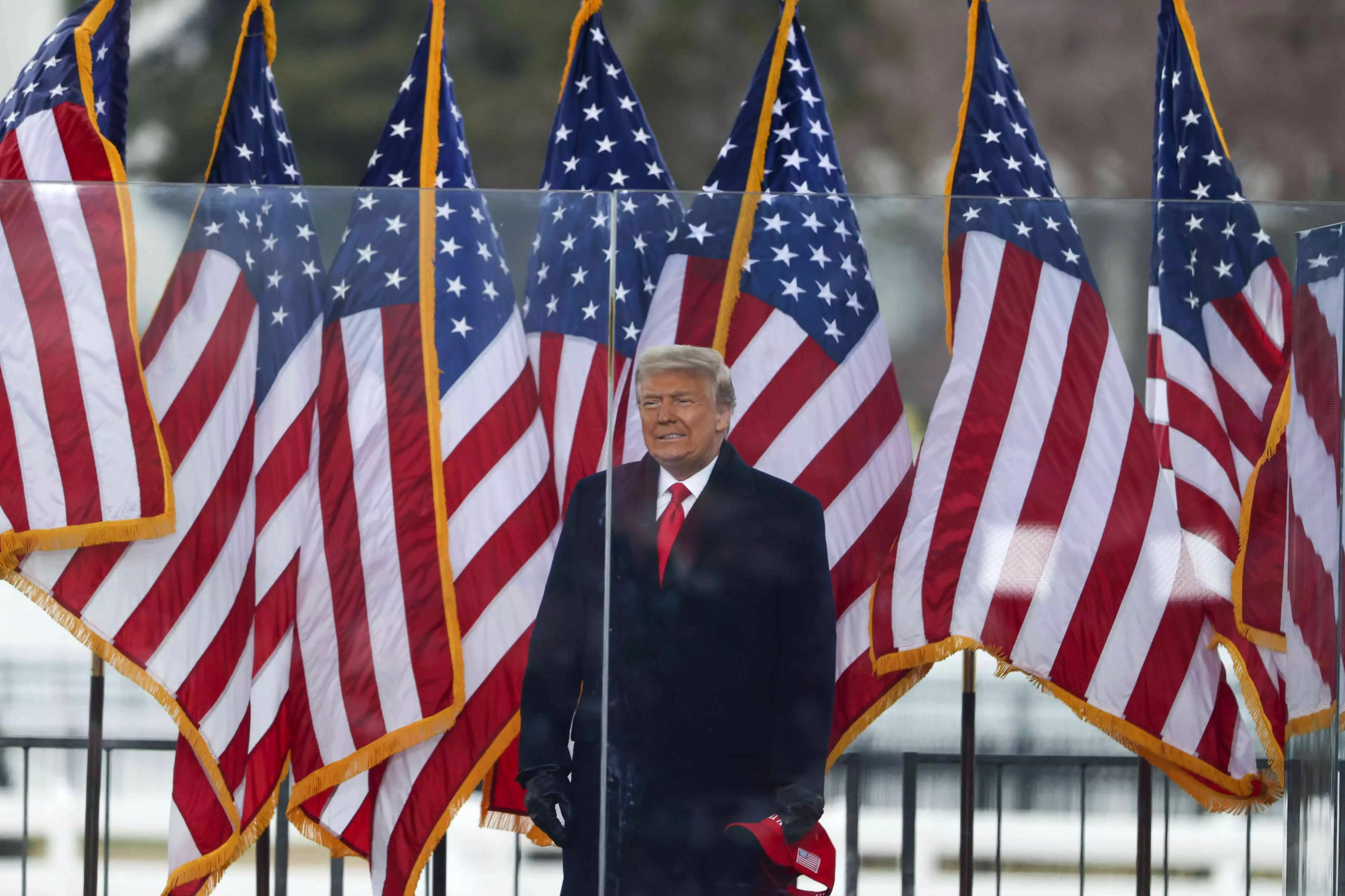 Tá Donald Trump ina sheasamh ar stáitse le bratacha Mheiriceá taobh thiar dó