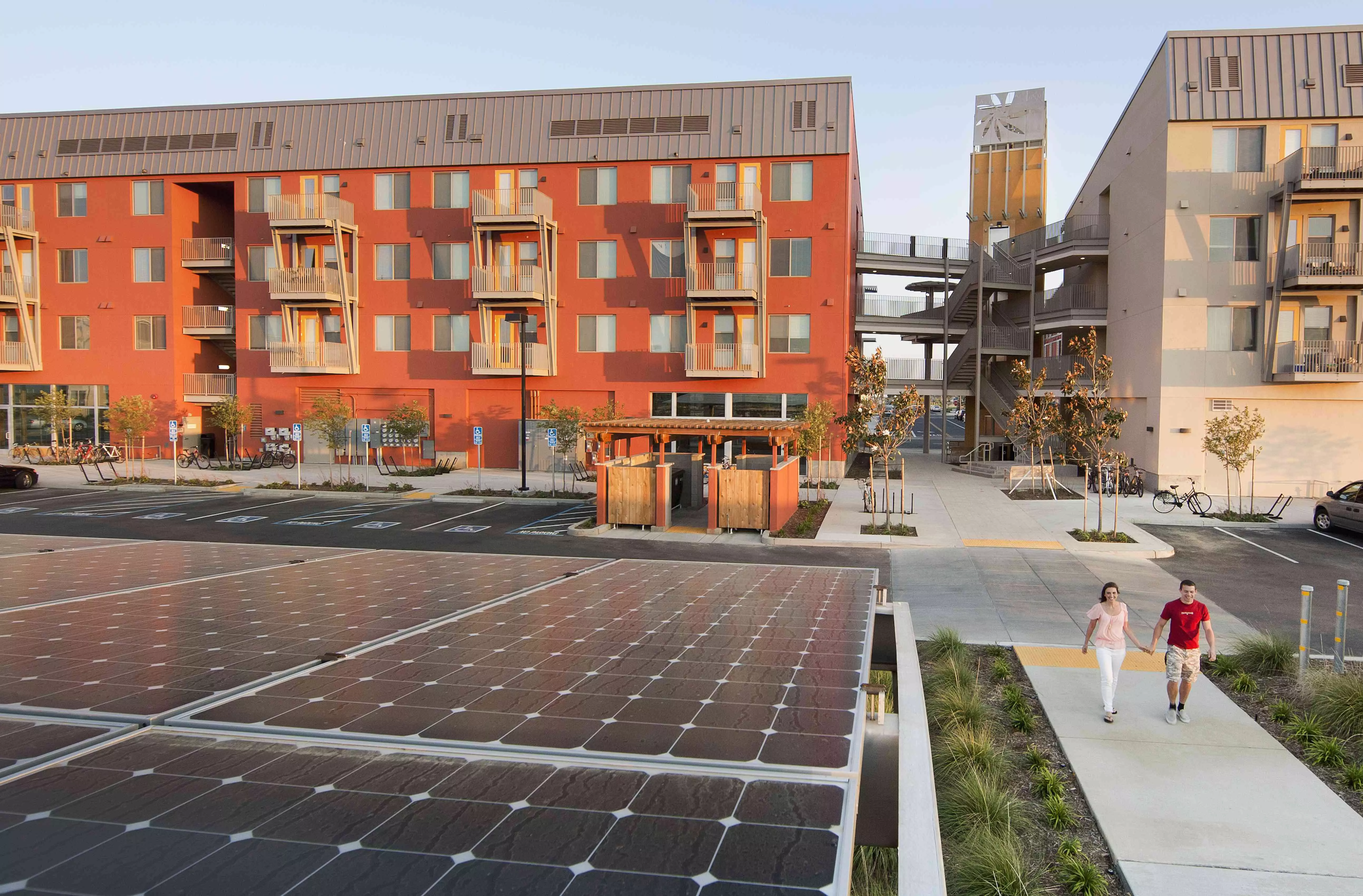 Två personer som går nära gröna byggnader och solpaneler, i en Zero Net Energy-gemenskap
