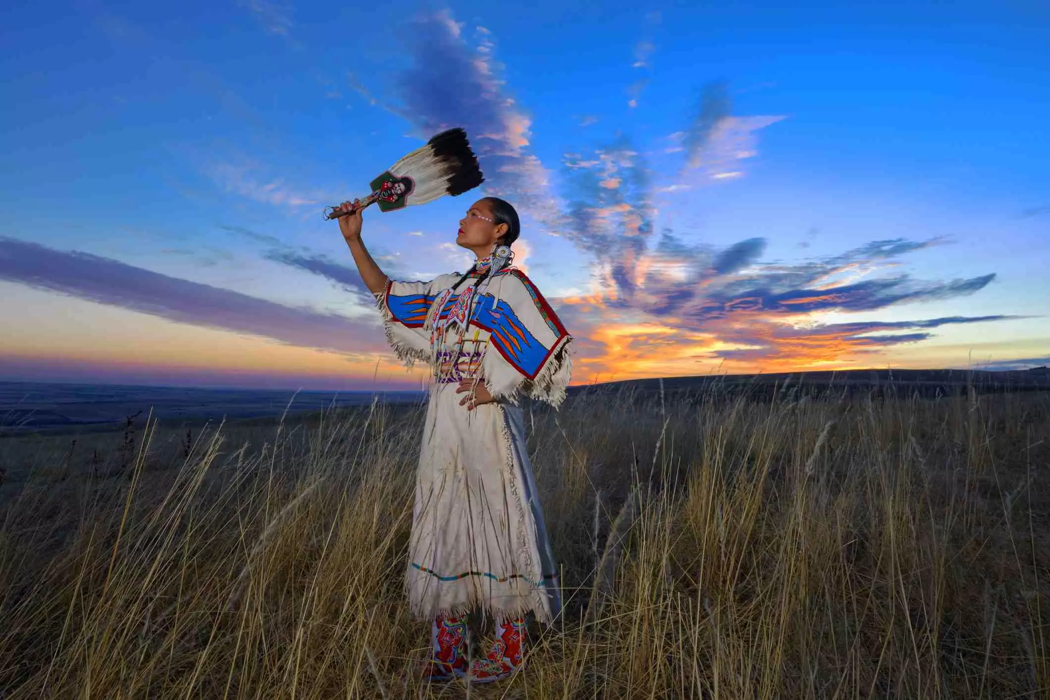 Femme amérindienne en costume traditionnel debout parmi l'herbe dans la prairie