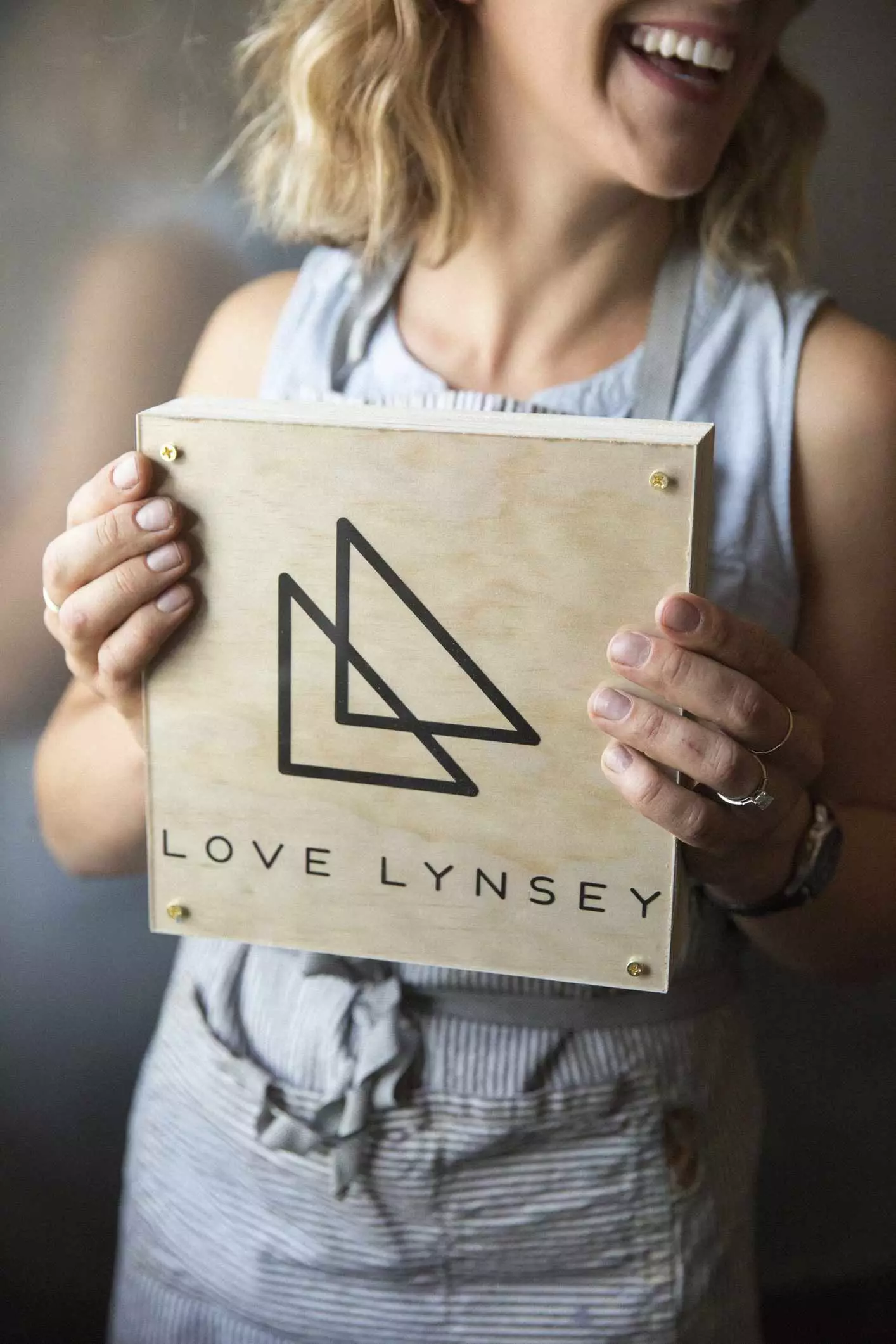 Een vrouw met een houten bordje met haar logo erop