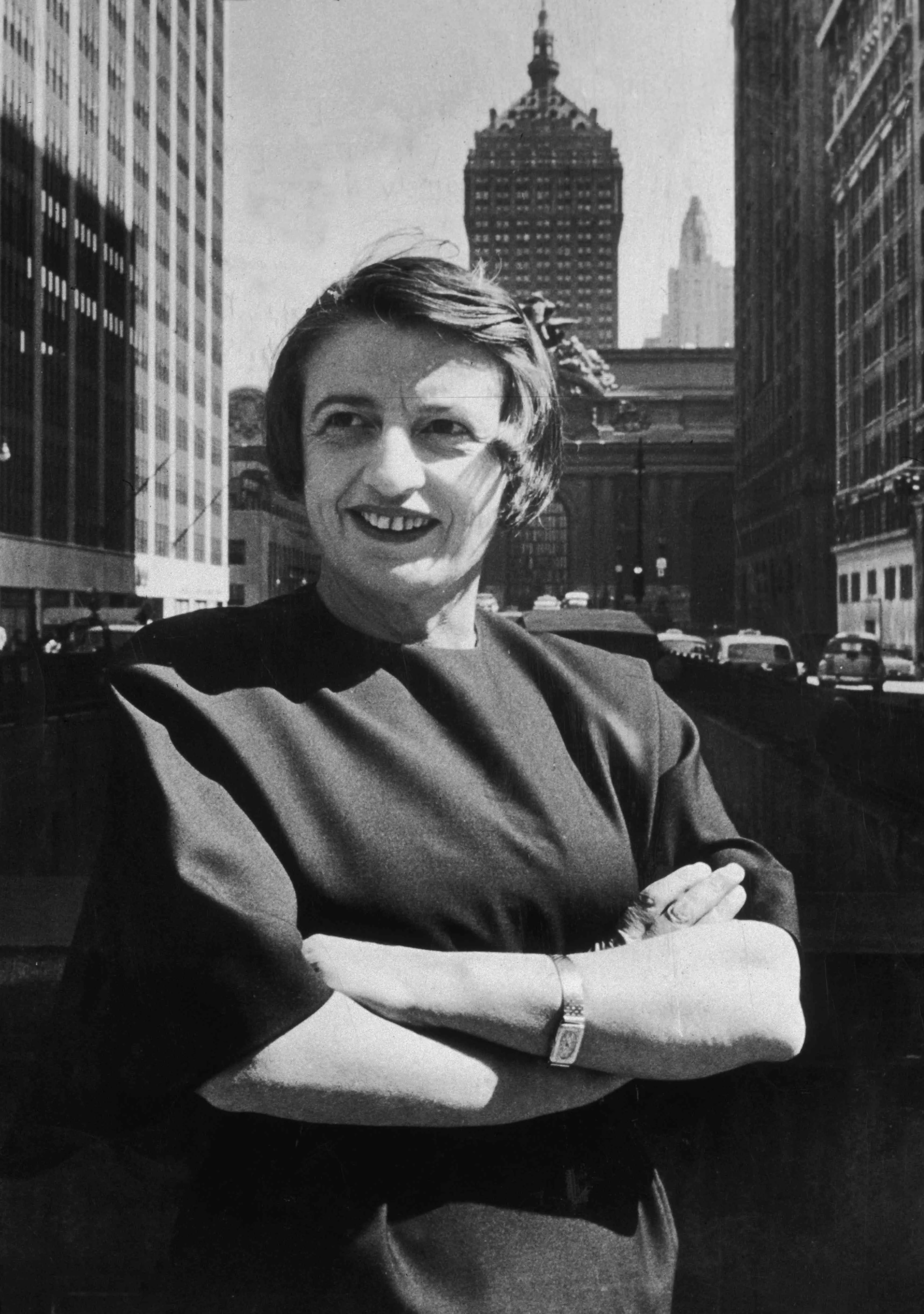 Ayn Rand estatubatuar idazle eta filosofo estatubatuarra, irribarre egiten du eta kanpoan zutik dago besoak gurutzatuta, Grand Central eraikinaren aurrean, Manhattan erdialdean, New York hirian.