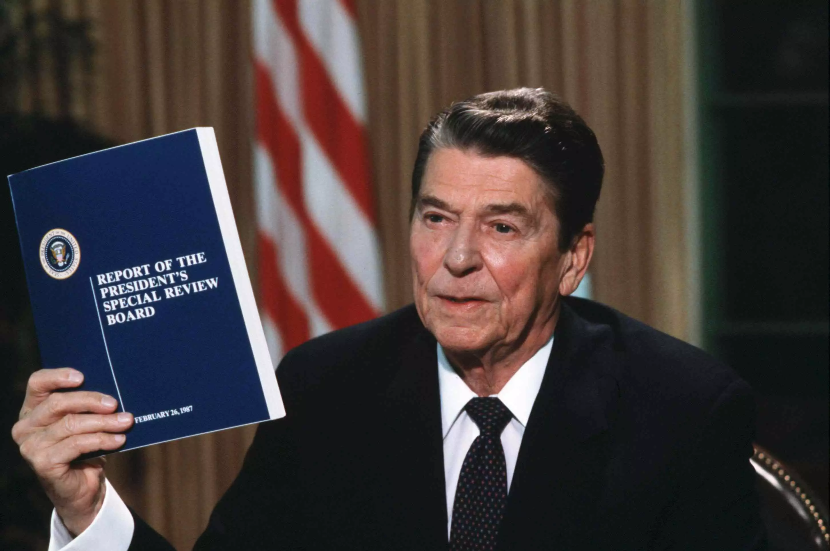 Presidenti Ronald Reagan mban një kopje të raportit të Komisionit të Kullës mbi skandalin Iran-Contra