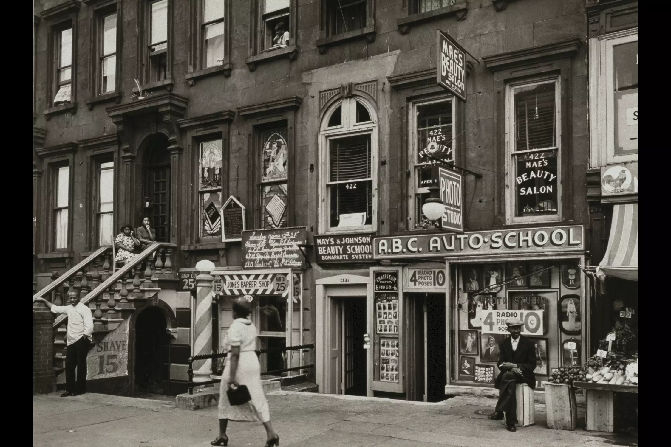 Wiwo awọn ile itaja lori 420 block of Lenox Avenue, Harlem, New York City, 14th Okudu 1938. Ile-itaja onigerun kan wa, ile-iwe ẹwa, ile-iwe adaṣe ati deli kan.