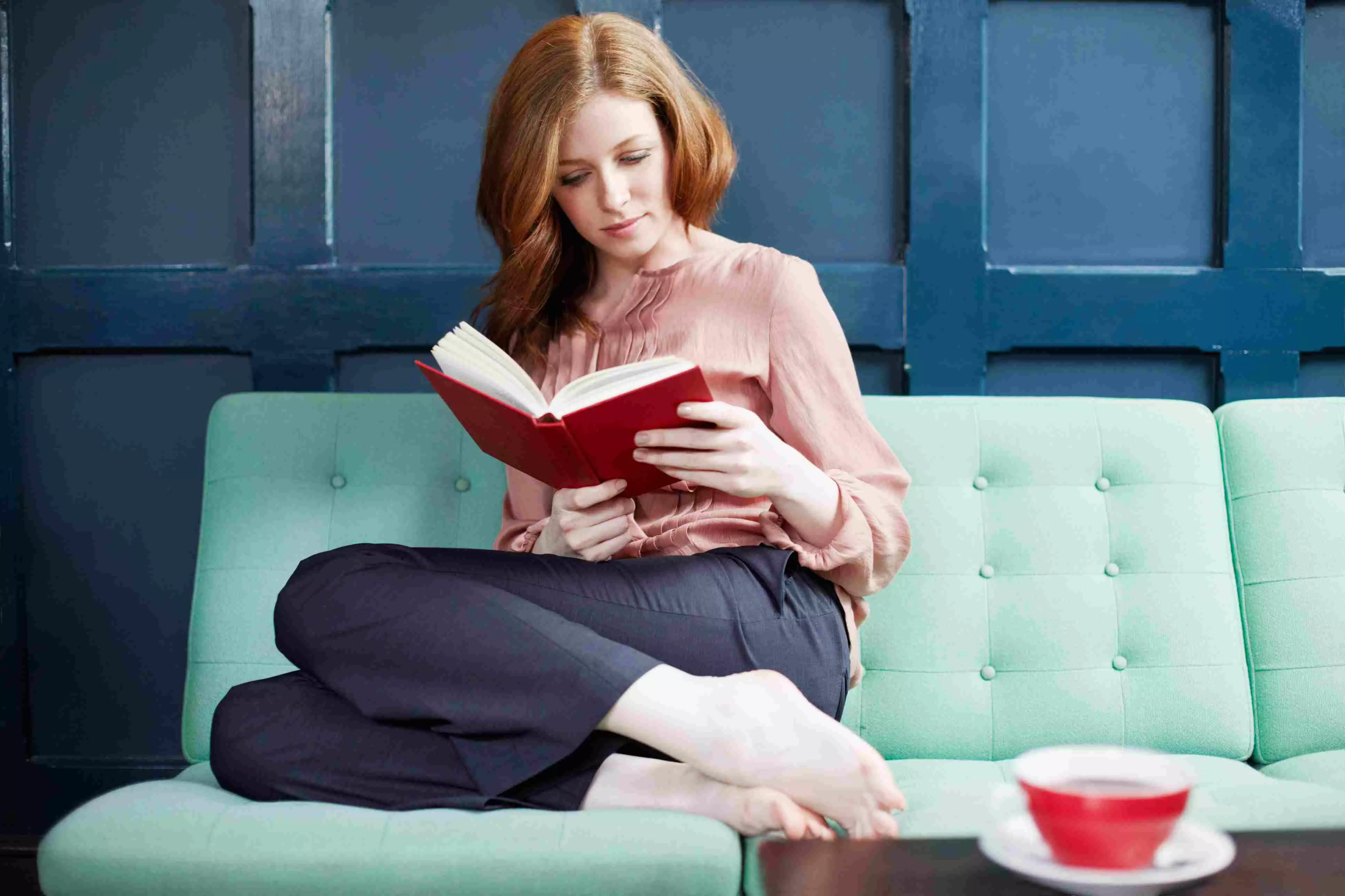 Wanita membaca buku di sofa.